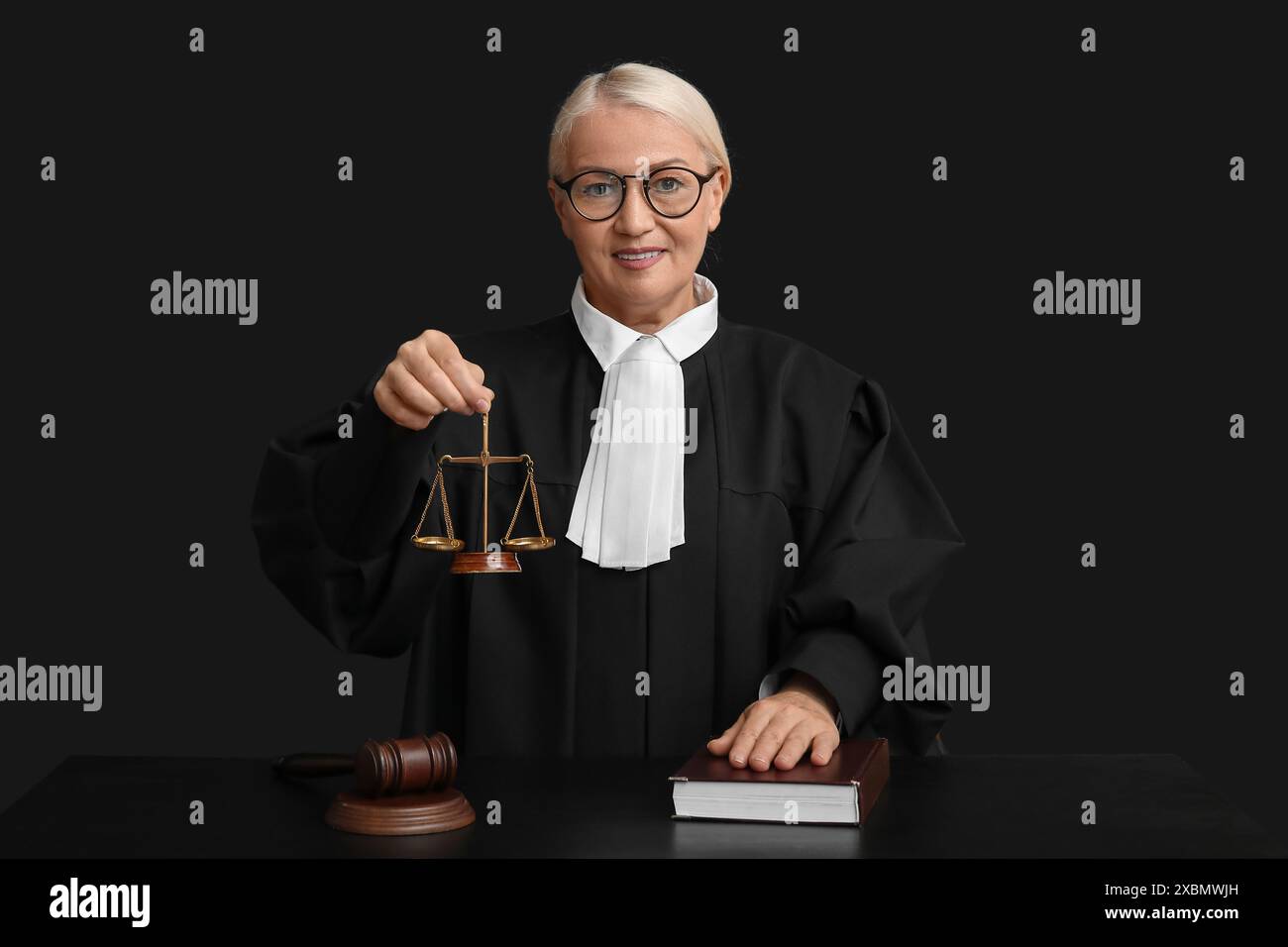 Mature female judge with scales of justice and book at table on black ...