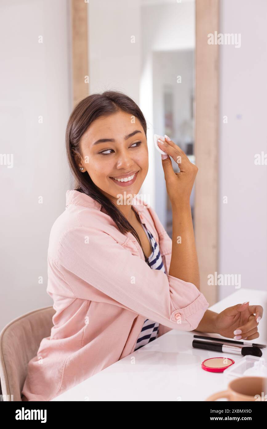 Happy biracial woman applying makeup, smiling while looking at her ...
