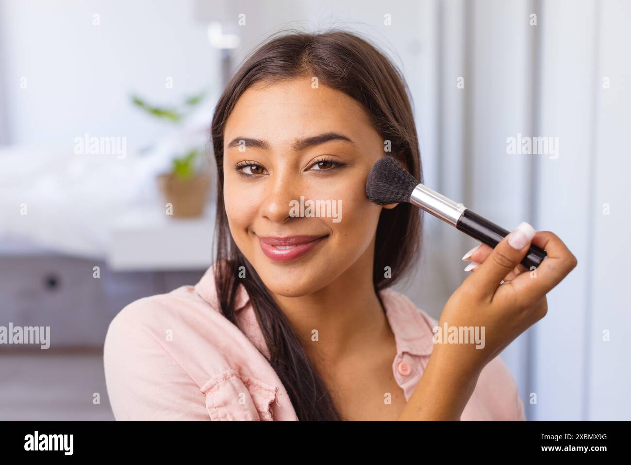 Happy biracial woman applying makeup with brush, smiling warmly Stock ...