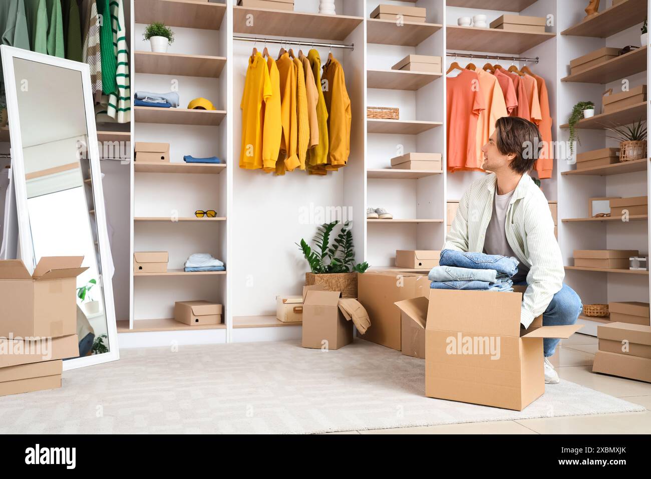 Handsome young happy man unpacking wardrobe boxes with stylish jeans in ...