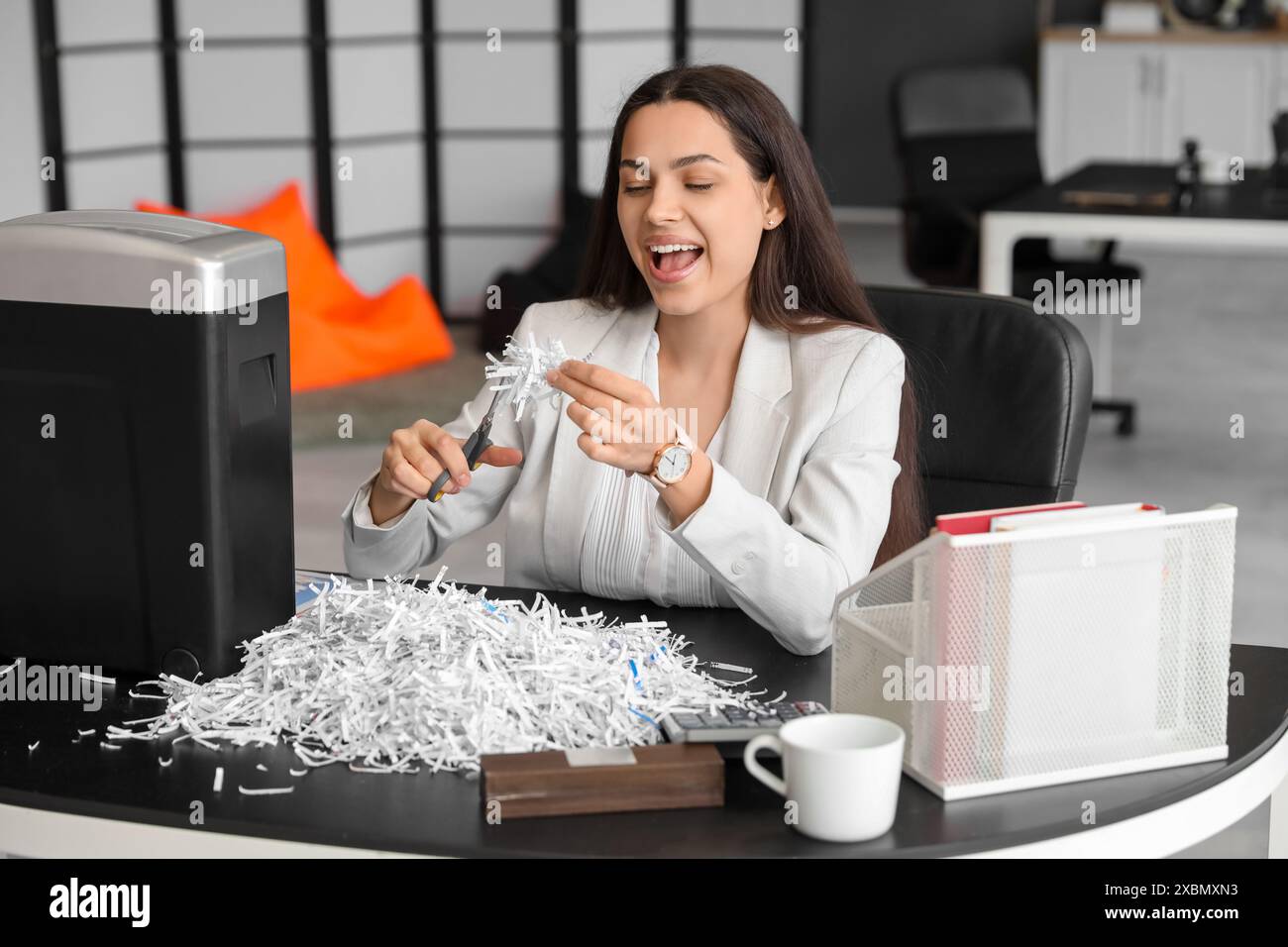 Young secretary with scissors, shredded paper and shredder in office ...