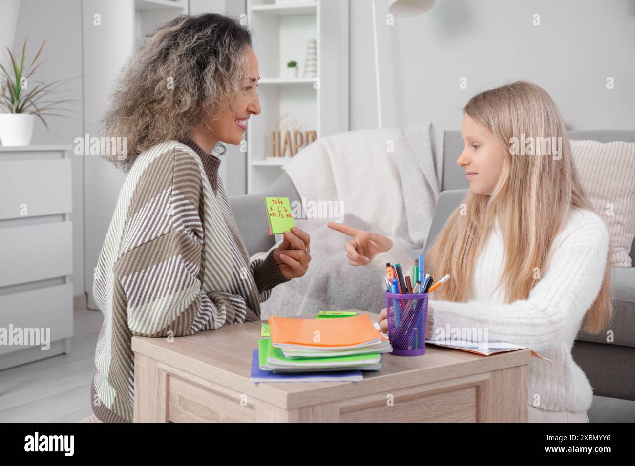 Female tutor with sticky note giving English lesson to little girl at ...