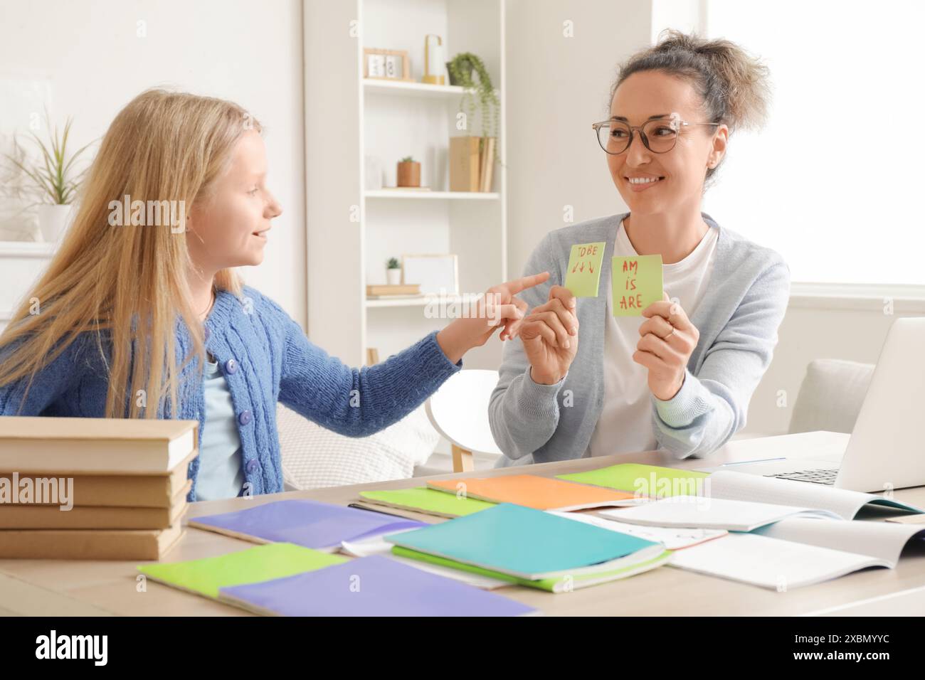 Female tutor with sticky notes giving English lesson to little girl at ...