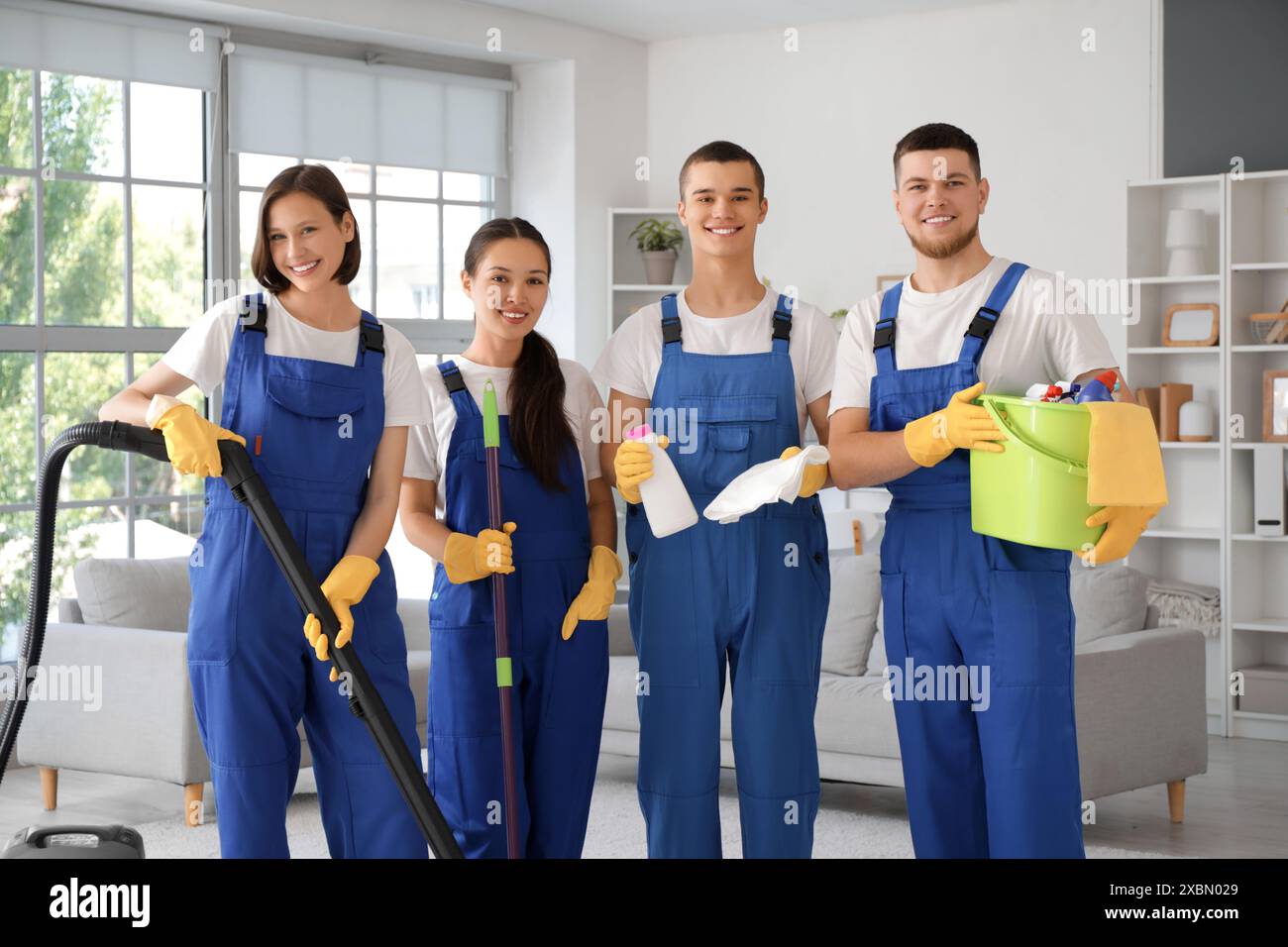 Team of young janitors with cleaning supplies in room Stock Photo - Alamy