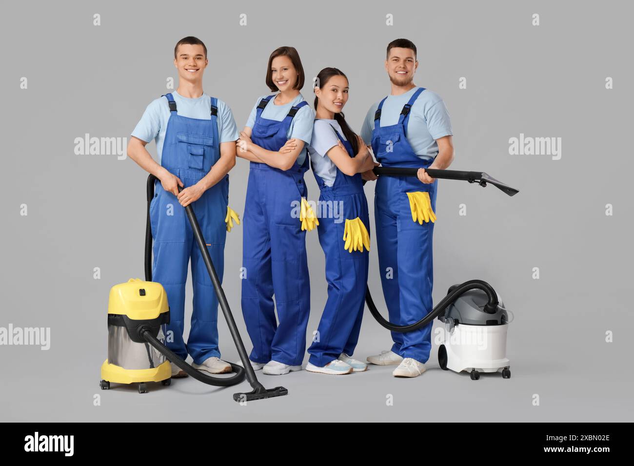 Group of young janitors with vacuum cleaners on grey background Stock ...
