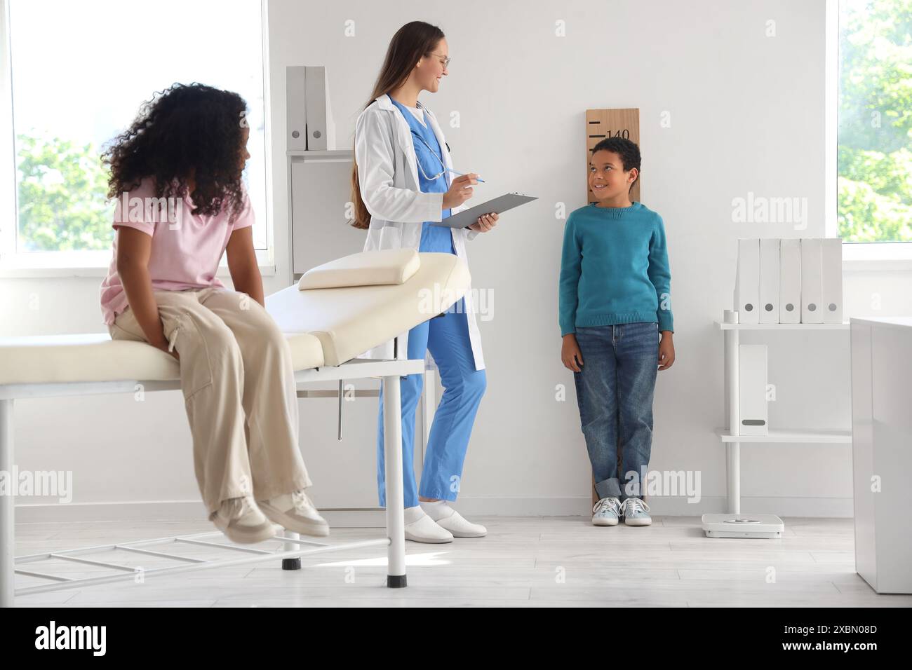 Female pediatrician with little African-American boy measuring height ...
