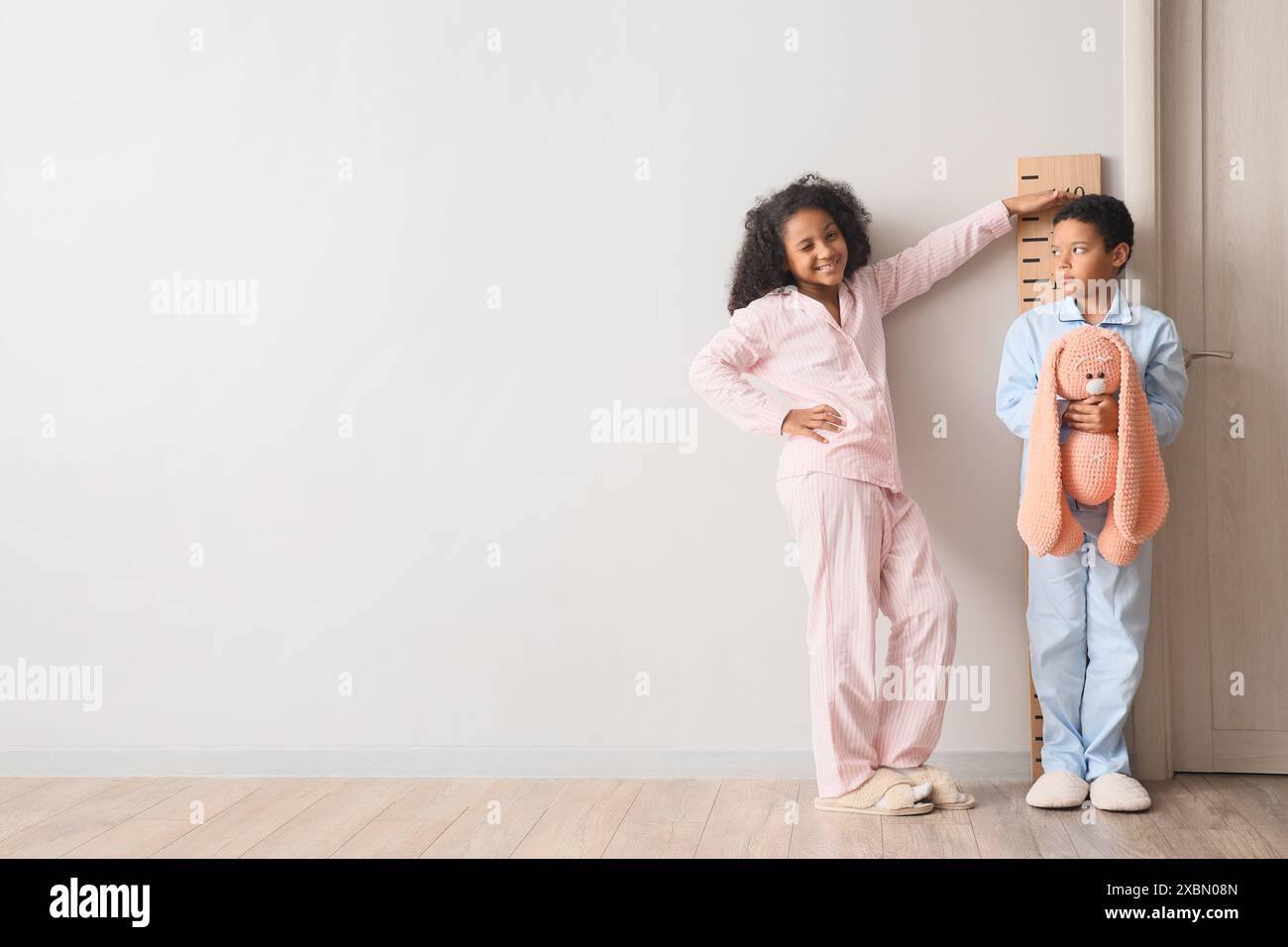 Little African-American girl measuring her brother's height near ...