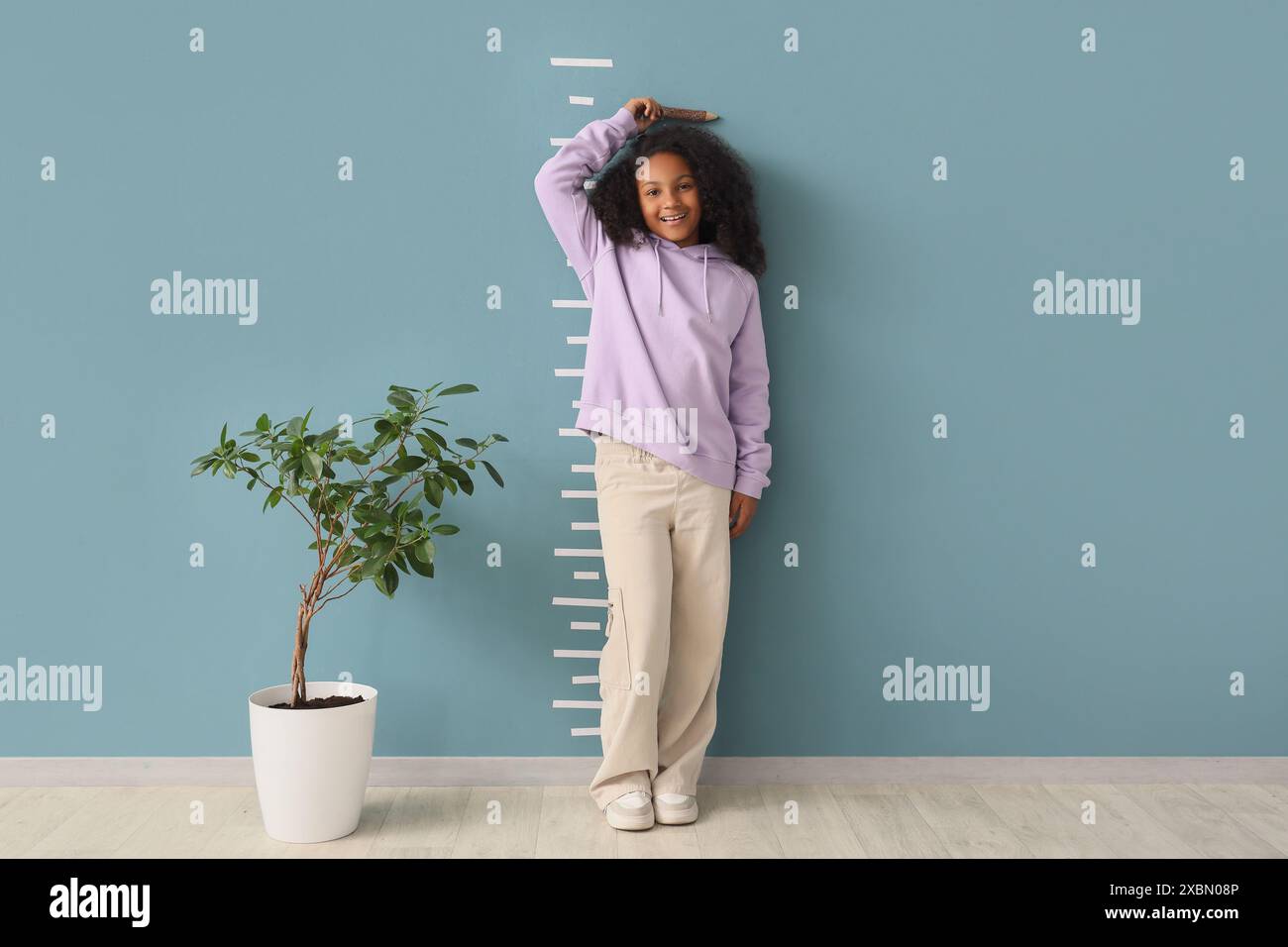Little African-American girl measuring height near blue wall Stock ...