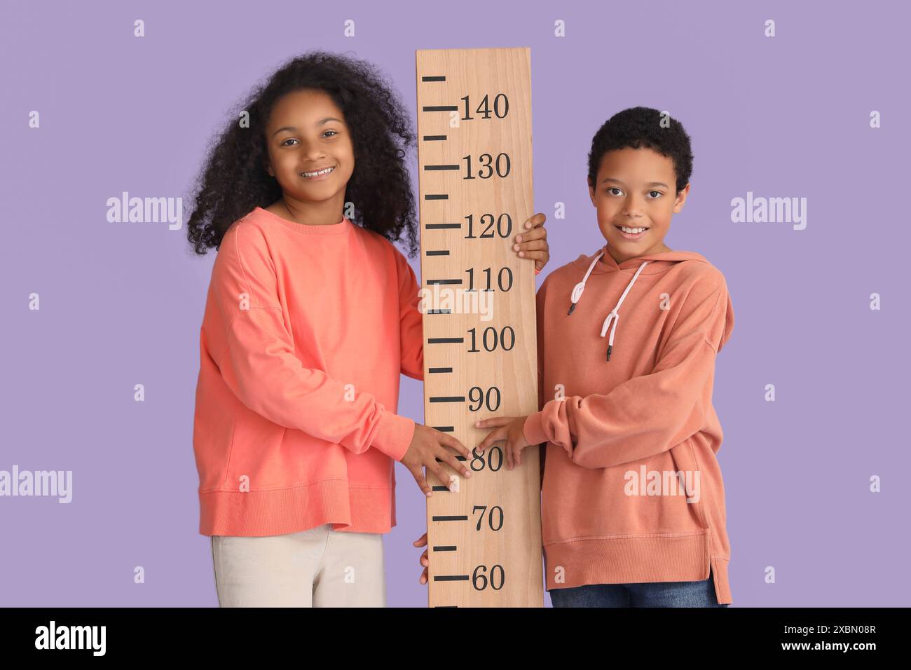 Little African-American children with stadiometer on lilac background ...