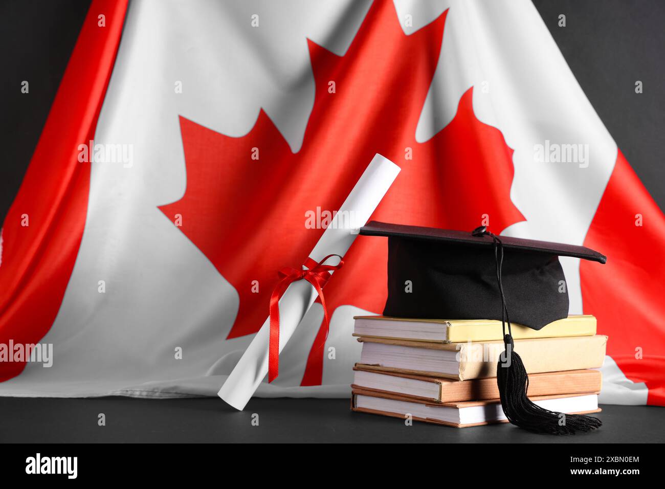 Stack of books, graduation hat, diploma and Canadian flag on dark ...