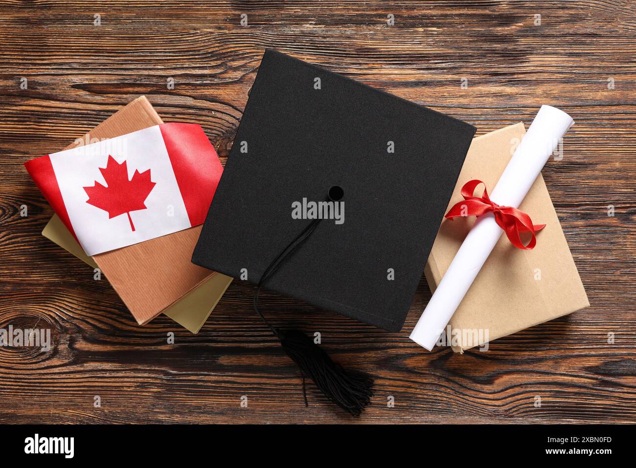 Graduation hat, diploma, books and Canadian flag on wooden background ...