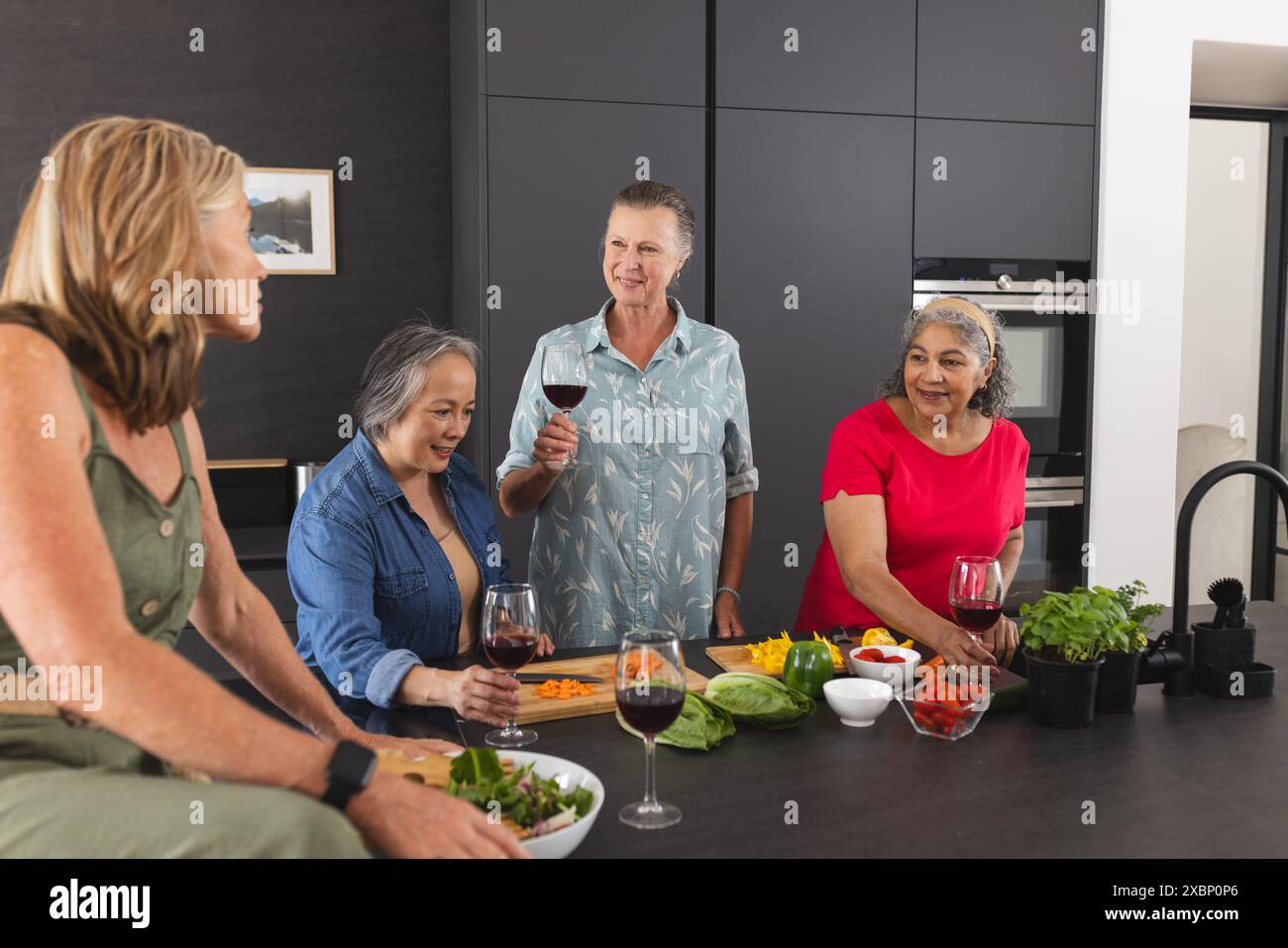 Diverse group of mature women enjoying wine and preparing food together ...