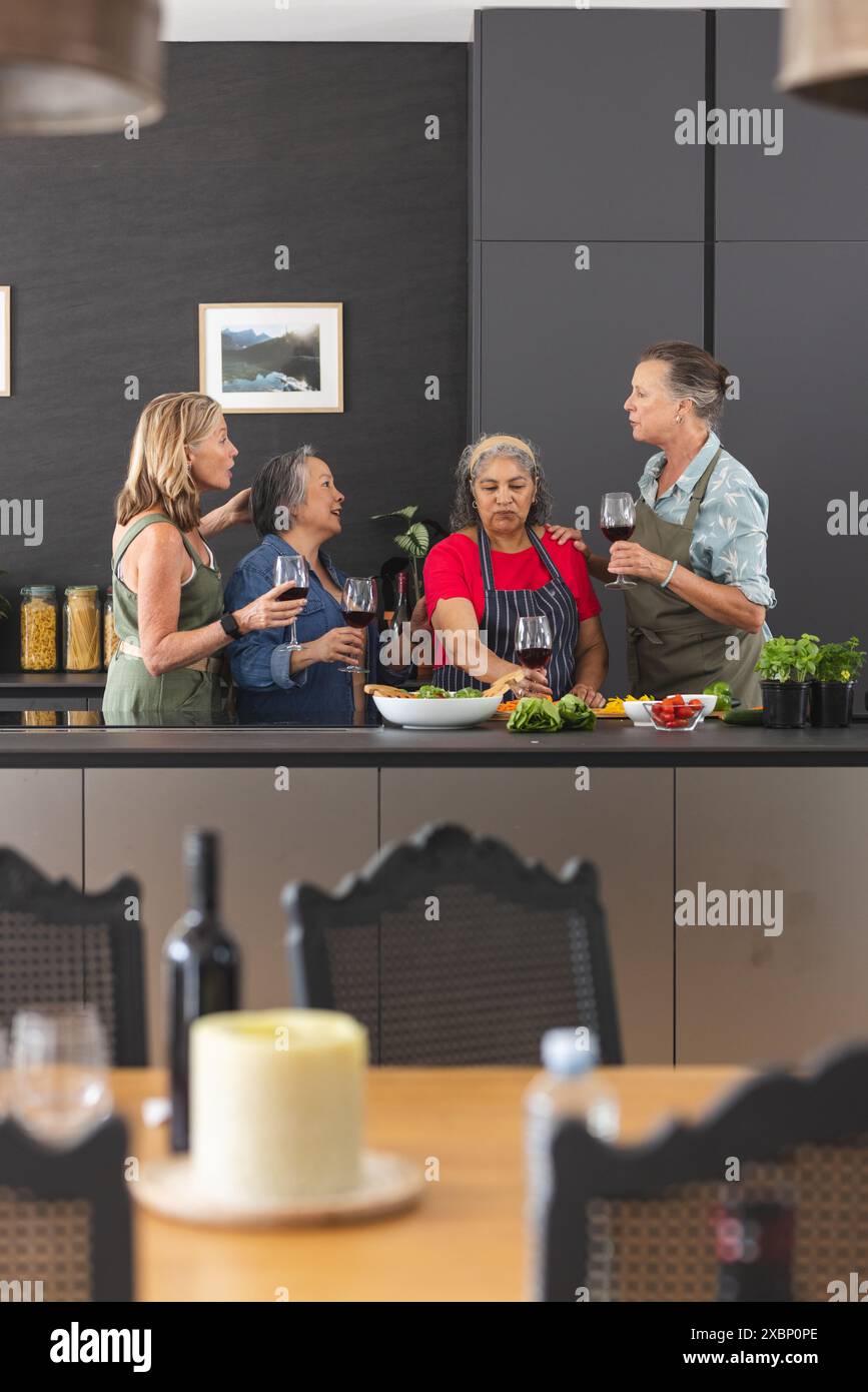 Diverse group of mature women enjoying wine and preparing food together ...