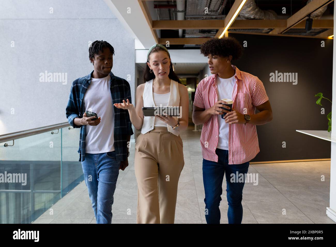 , diverse colleagues walk together as one shows a tablet; teamwork in a ...