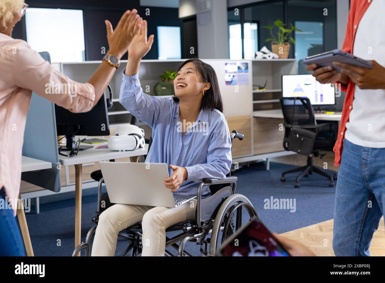 Business colleagues bond as an Asian woman in a wheelchair high-fives ...
