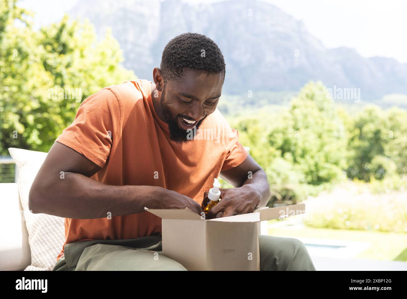 Young African American man opening package and smiling by a pool, at ...