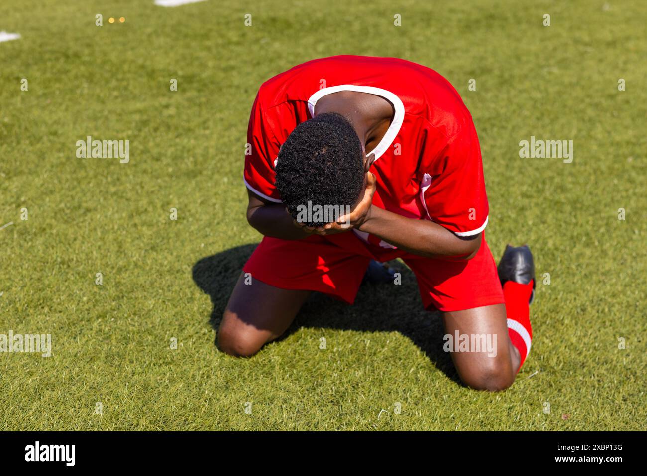 African American soccer player kneeling on grass field, looking down ...