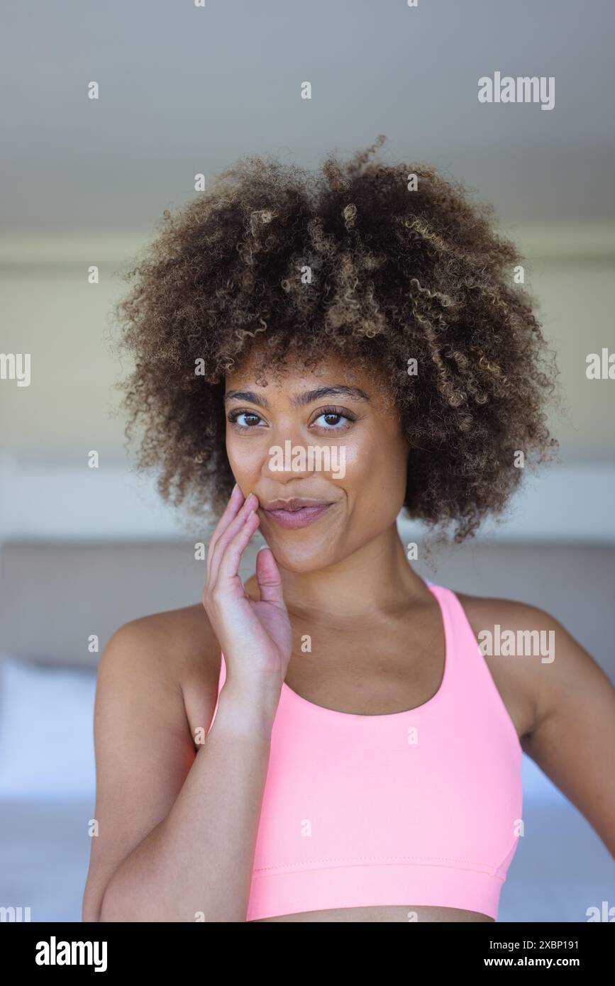 Happy biracial woman with curly hair wearing pink sports bra smiling ...