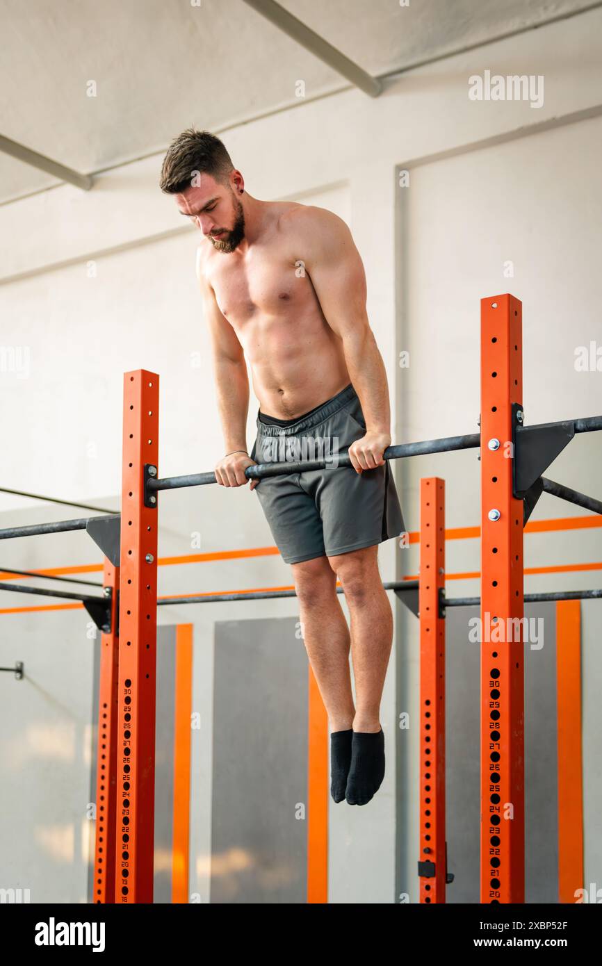 Focused male performing calisthenics muscle up high position on metal ...