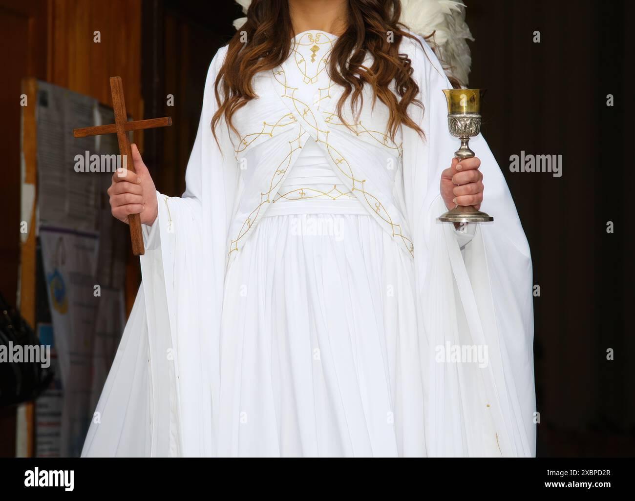 Woman wearing a white angel costume, holding a wooden cross and a metal ...