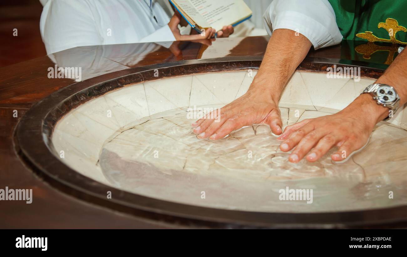 Priest performing a water blessing in a church's baptismal font during a religious ceremony ...