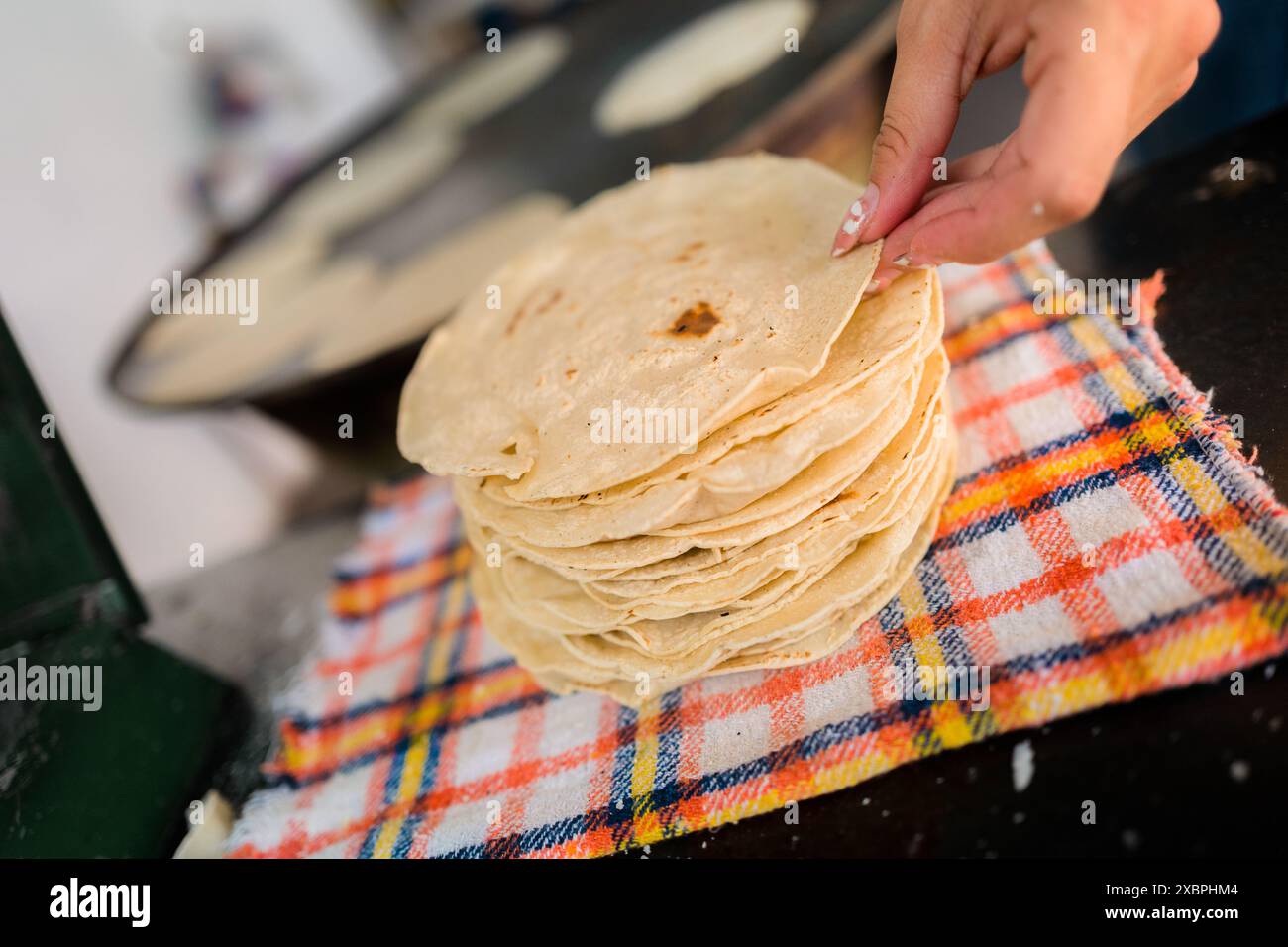 A Mexican cook stacks the freshly made tortillas in a pile in a ...