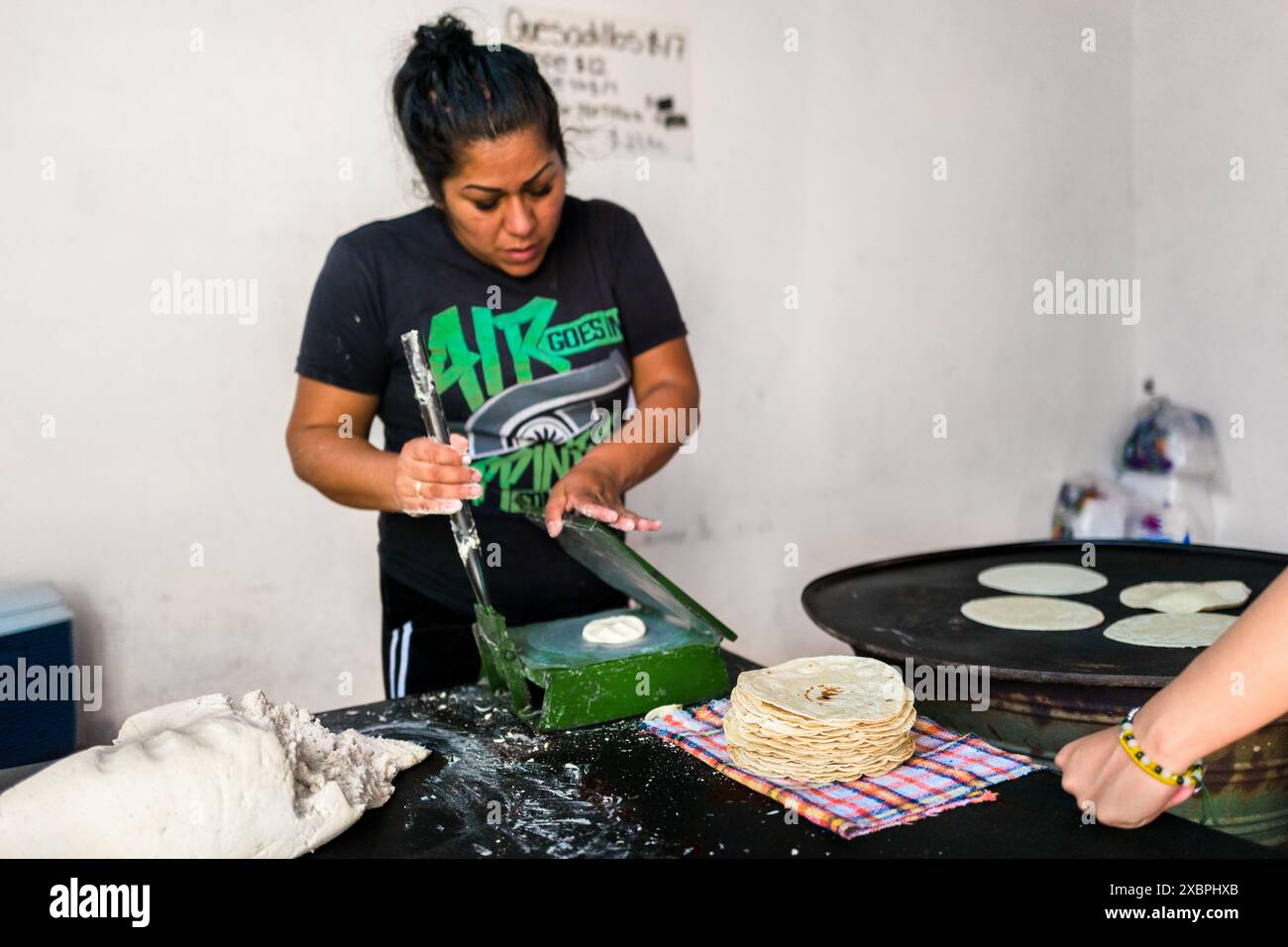 A Mexican cook prepares tortillas from dough on a tortilla press in a ...