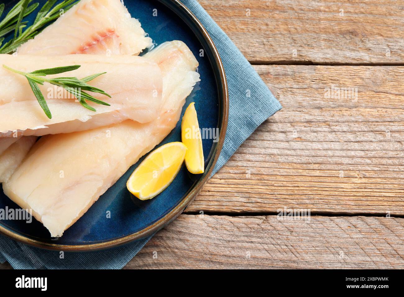 Pieces of raw cod fish, rosemary and lemon on wooden table, top view ...