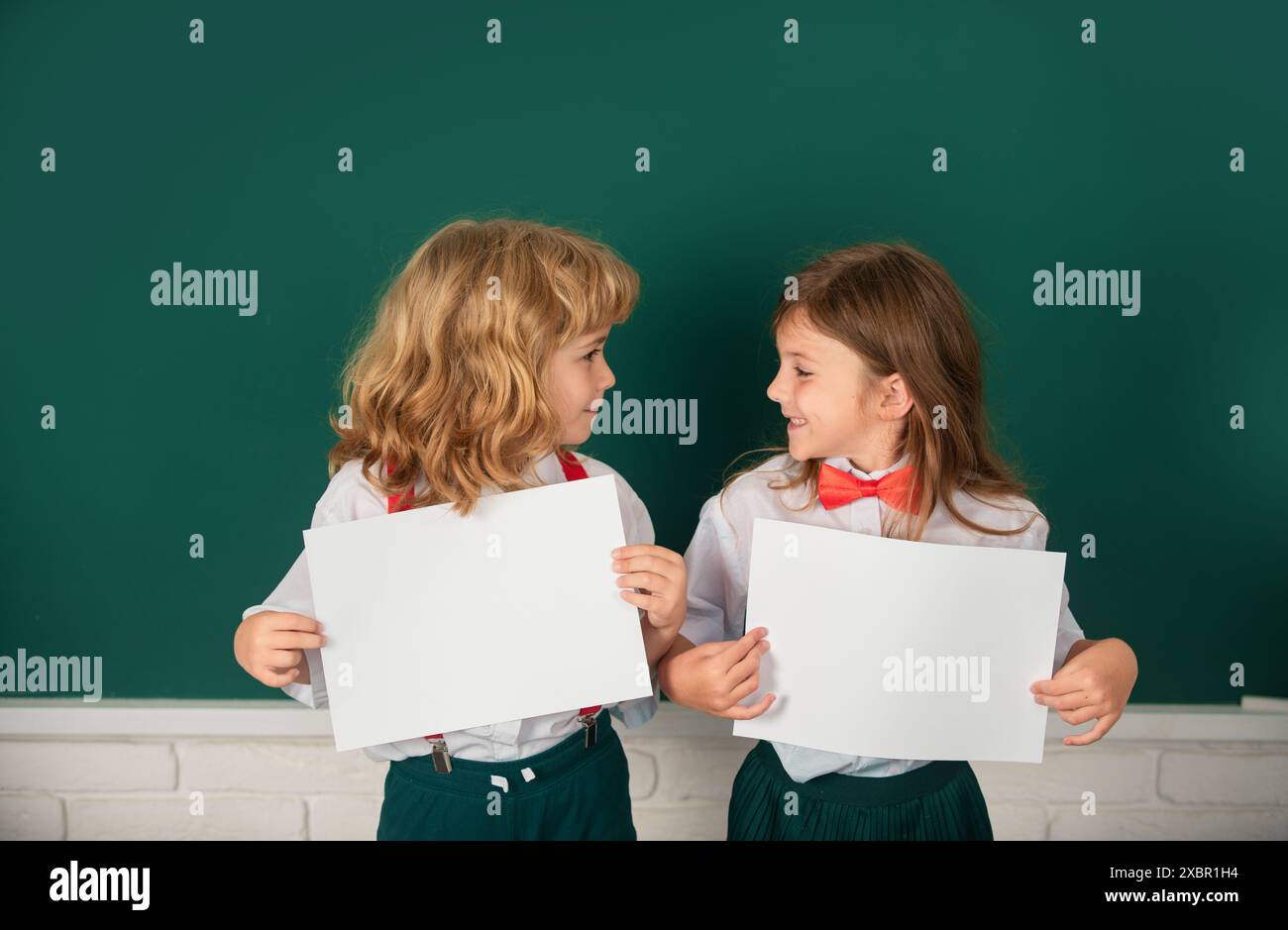 Two schoolkids holding white paper blank, poster with copy space ...