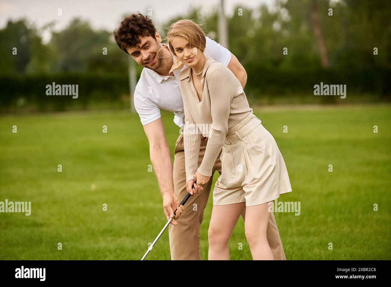 A young man and woman in elegant attire playing golf on a lush green ...