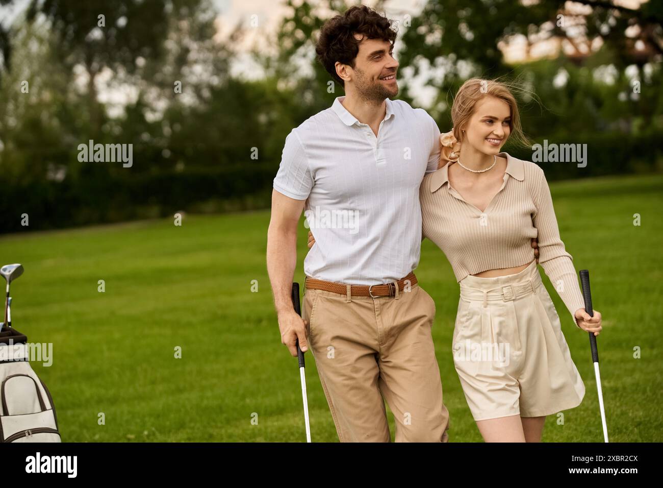 A young couple, elegantly dressed, walk on a golf course, enjoying each ...