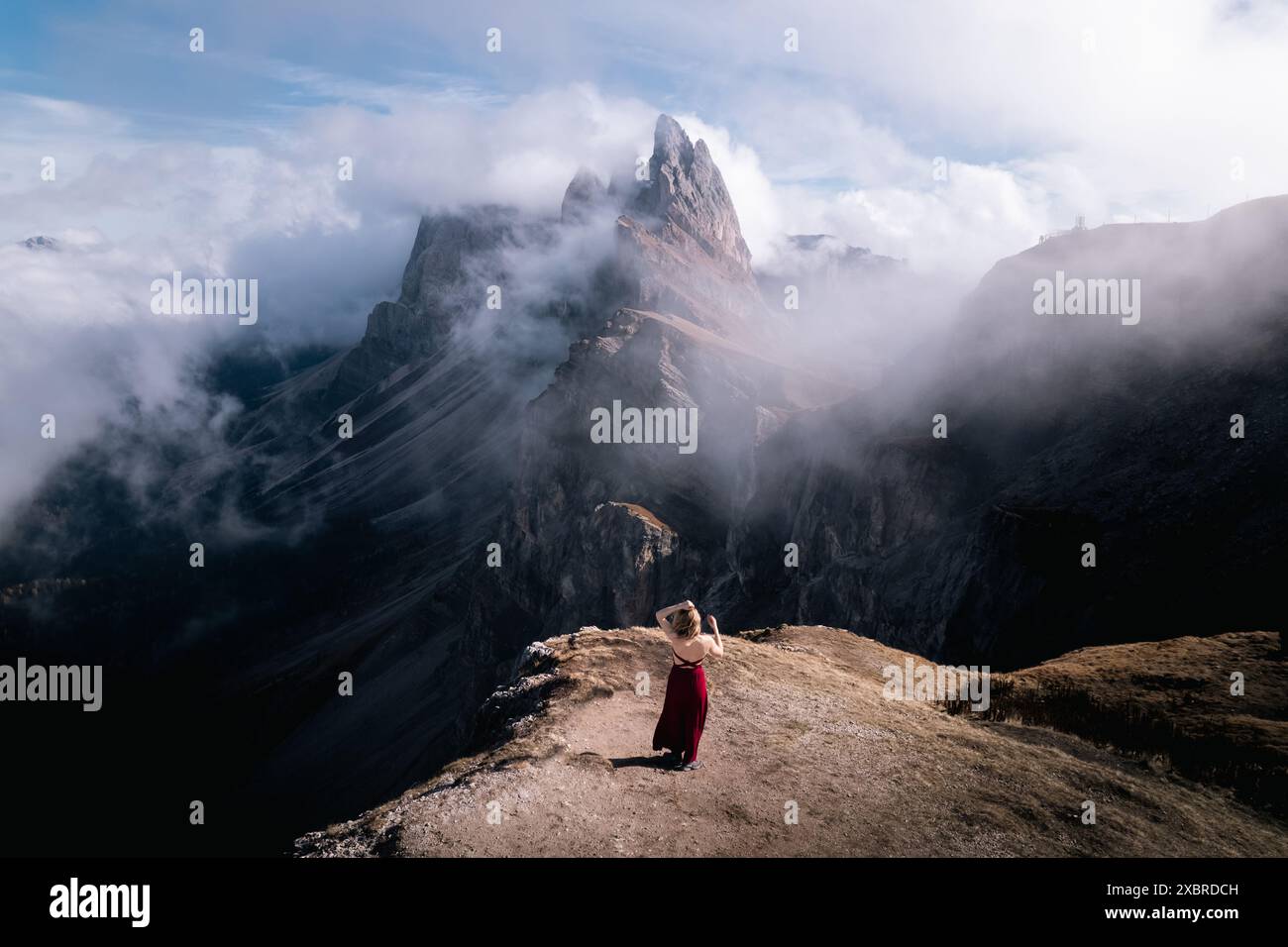 A single beautiful girl in a red dress stands facing the mountain ...