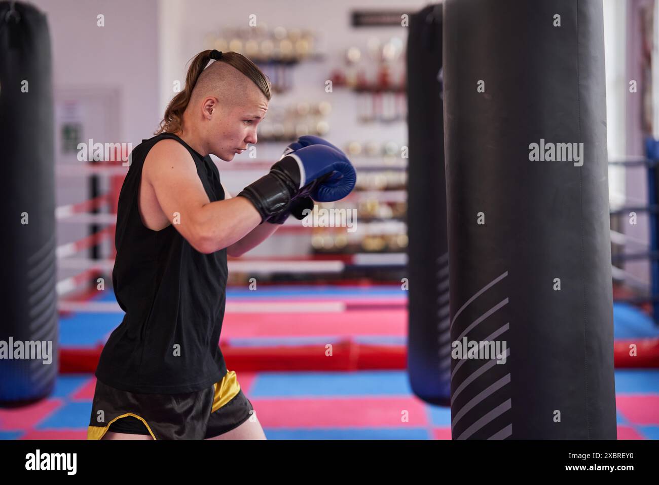 Young kickboxer training on the heavy bag in the gym, the ring is in ...