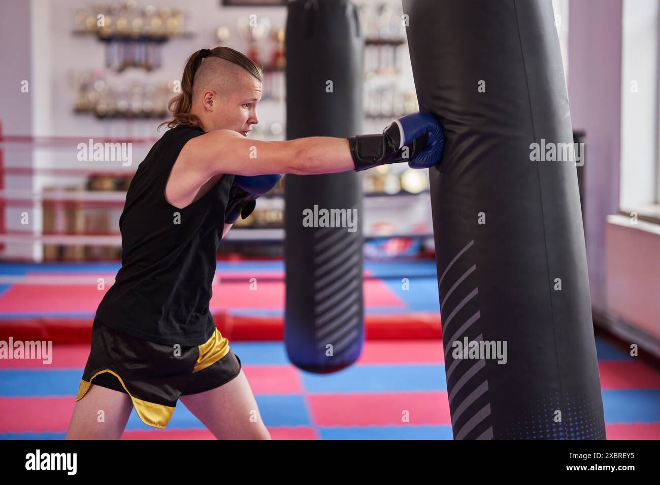 Young kickboxer training on the heavy bag in the gym, the ring is in ...