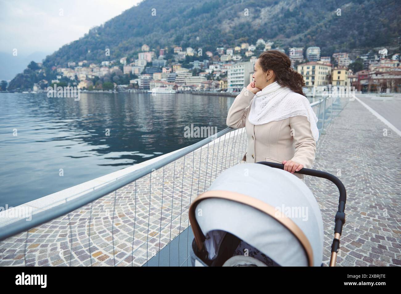A woman strolls along a picturesque lakeside promenade with a baby ...