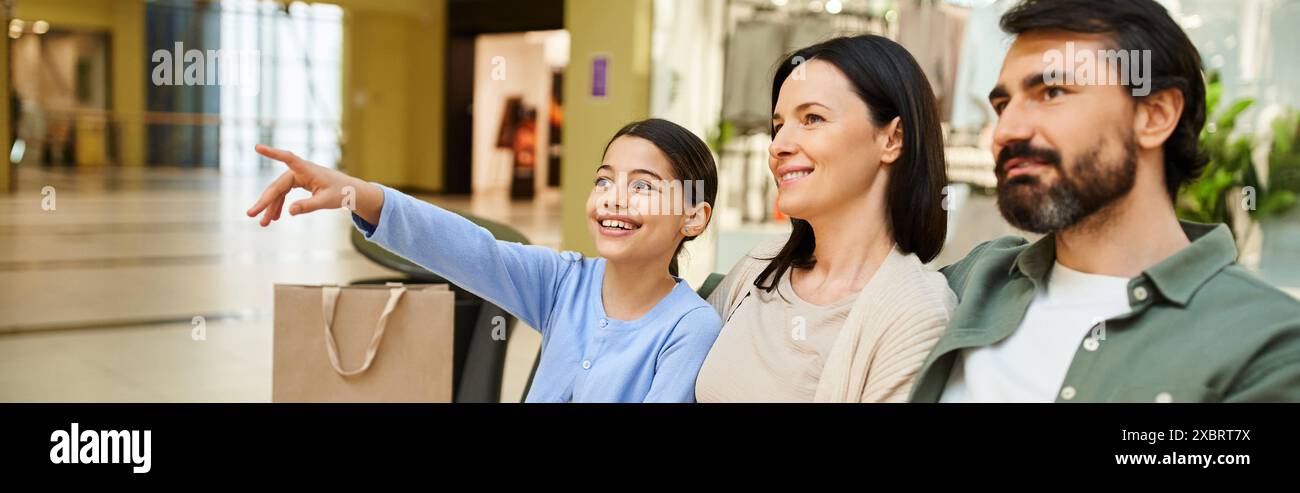 A happy family sits in a shopping mall, with a child pointing excitedly ...