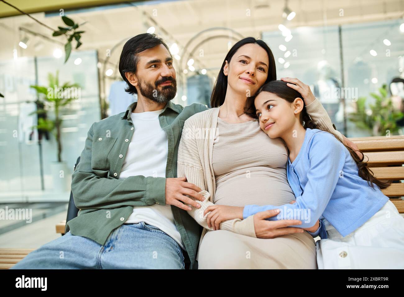 A pregnant woman and her daughter sit on a bench, sharing a quiet moment together in a bustling ...