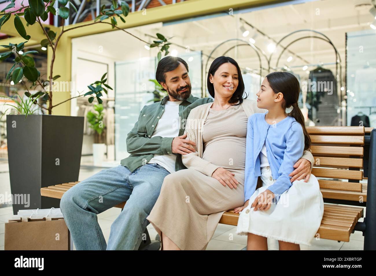A cheerful family enjoys a shopping day, sitting together on a bench in ...