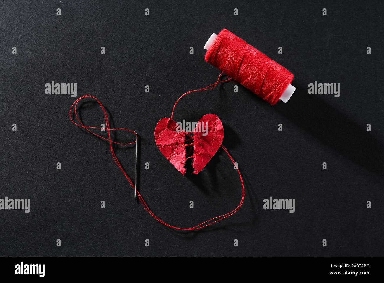 Halves of torn paper heart connected by thread on black background ...