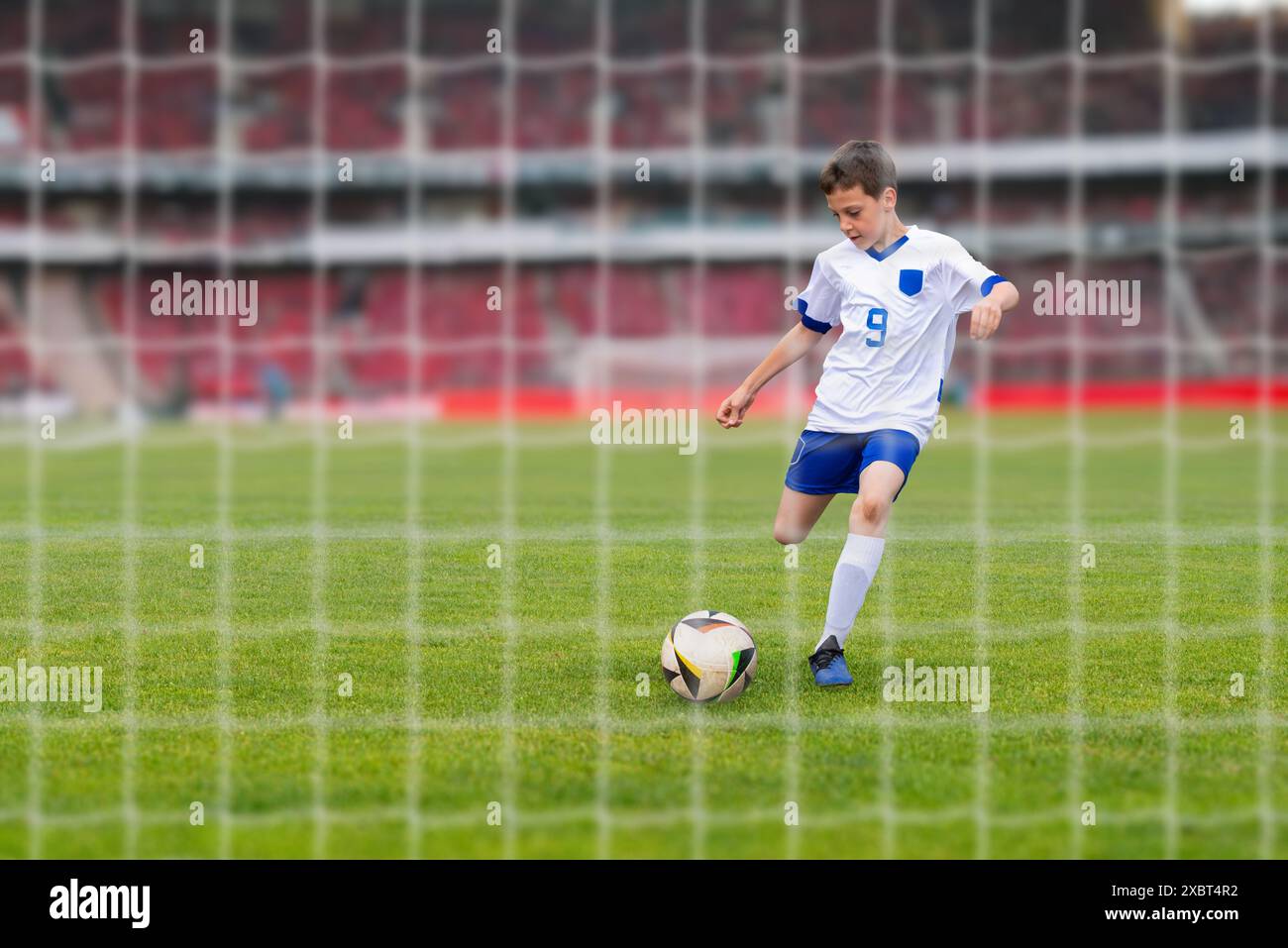 Young soccer player in a white dress shooting towards the goal on a ...