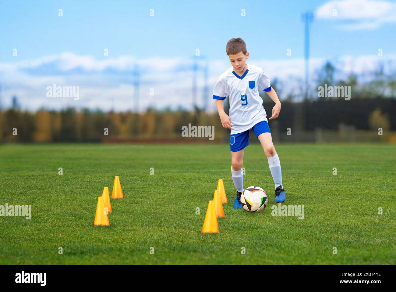 Young boy practices football by maneuvering around cones in a training ...