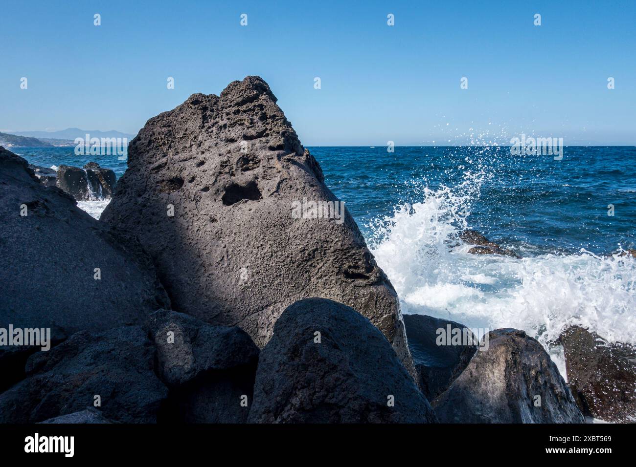 A beach of black volcanic basalt rock on the east coast of Sicily, near ...