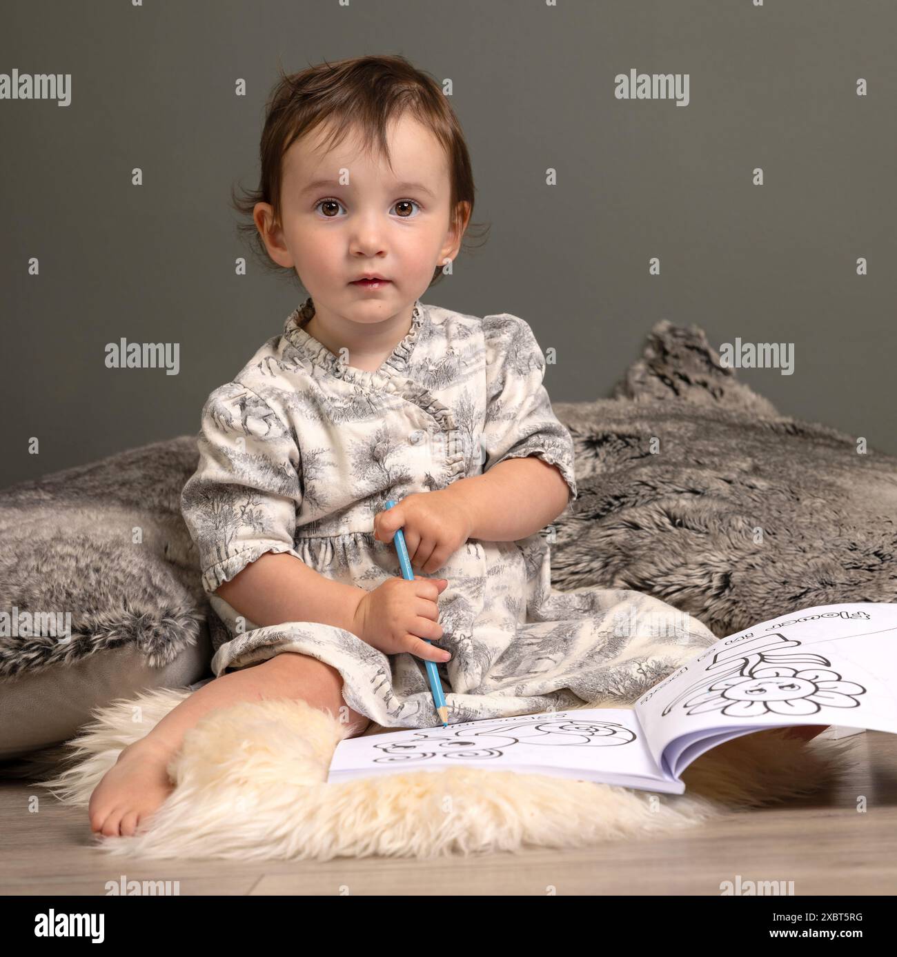 Portrait of a cute ittle girl sitting on the floor on a sheepskin rug ...
