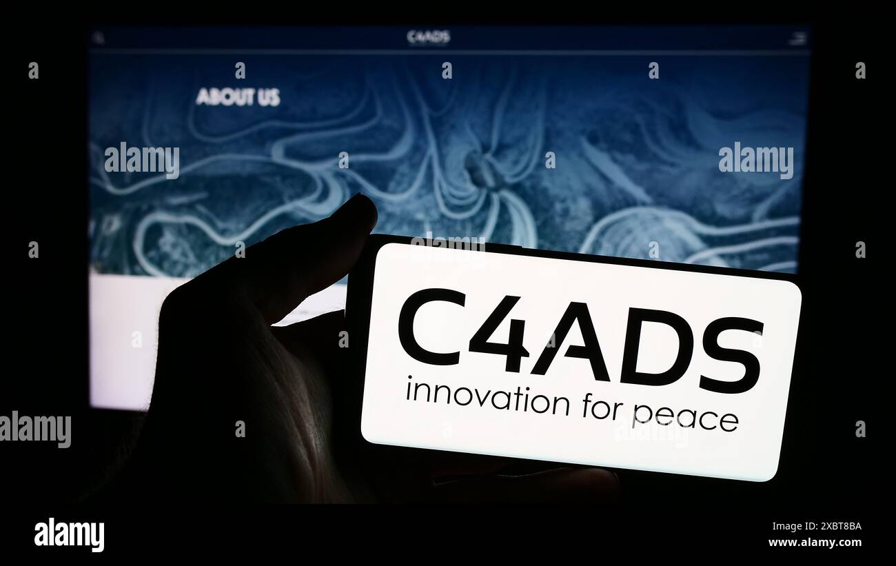 Person holding smartphone with logo of Center for Advanced Defense Studies (C4ADS) in front of ...