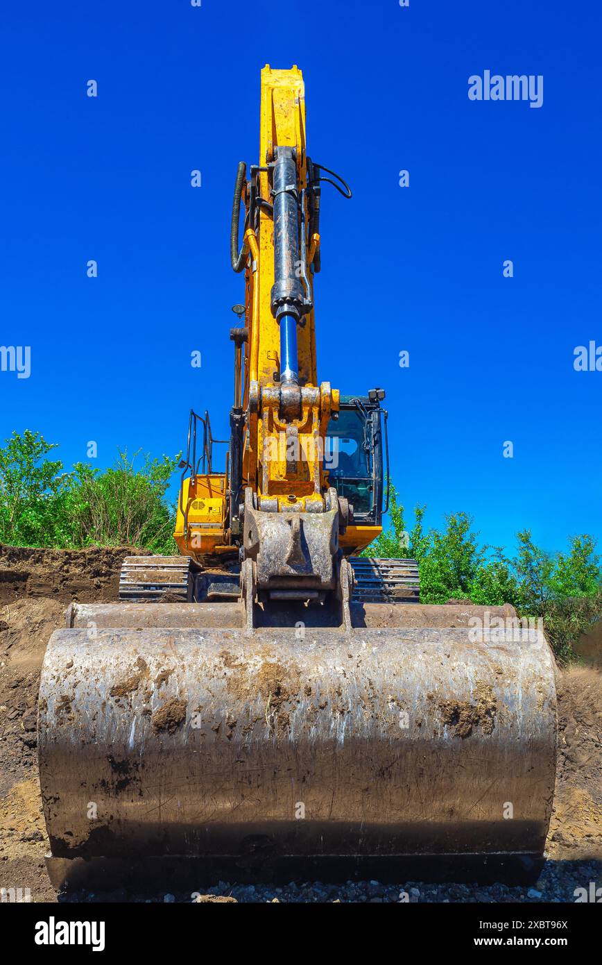 Front view of yellow excavator bucket against blue sky. Close ...