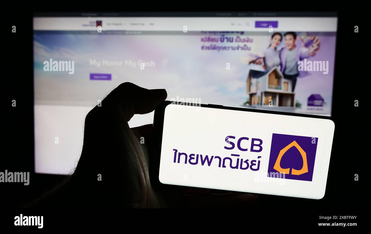 Person holding mobile phone with logo of The Siam Commercial Bank Public Company Limited (SCB ...