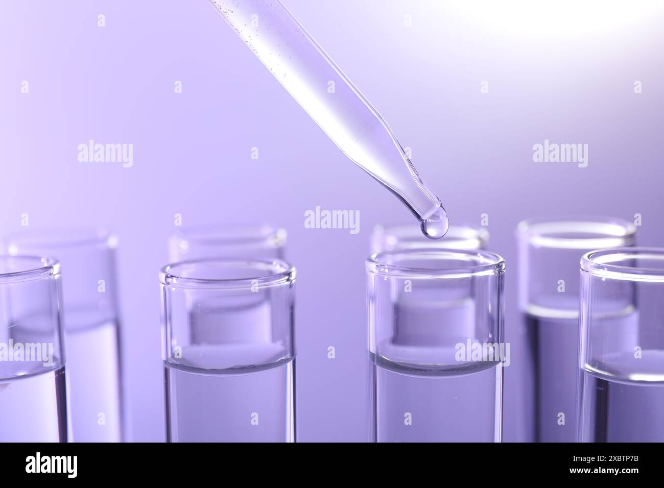Dripping liquid from pipette into test tube on violet background ...
