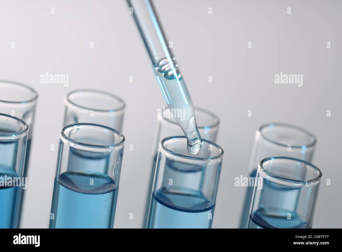 Dripping light blue liquid from pipette into test tube on gray ...