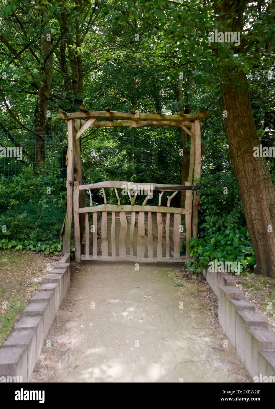 A rustic wooden gate at the entrance of a lush green park with trees ...