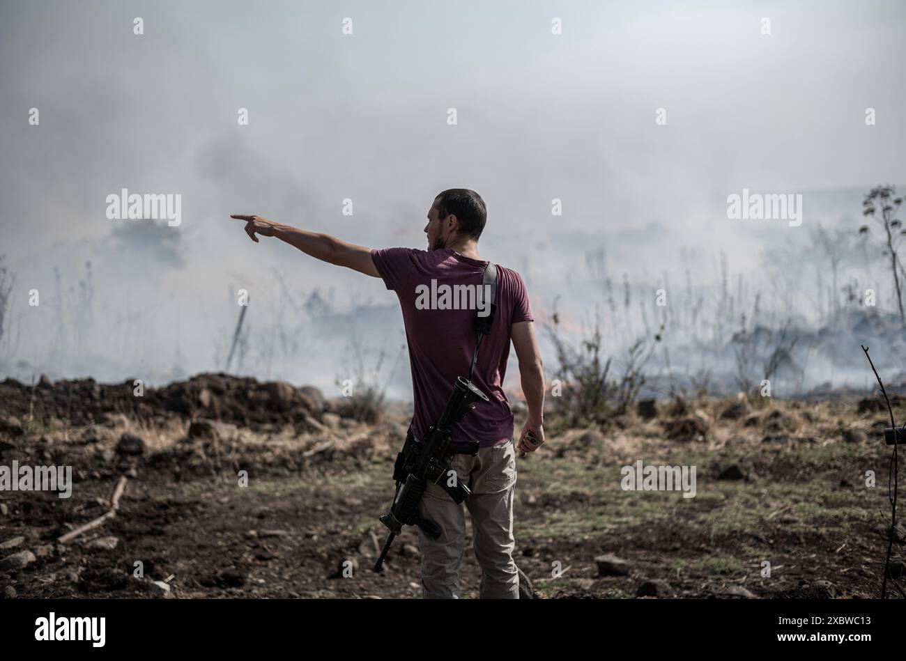 Qatsrin, Israel. 13th June, 2024. An armed man stands near a fire ...